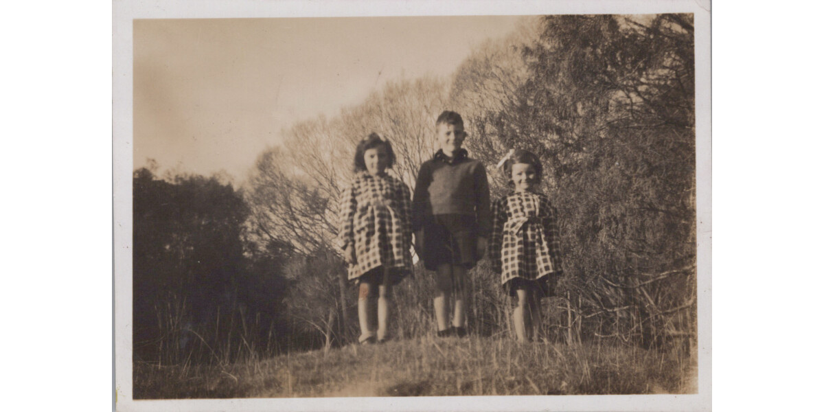 Portrait of three children standing in front of trees