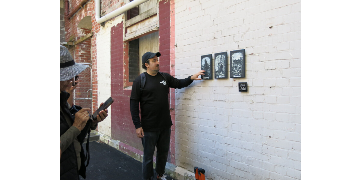 Dr Reuben Woods points at work by Dark Ballad | discoverywall.nz